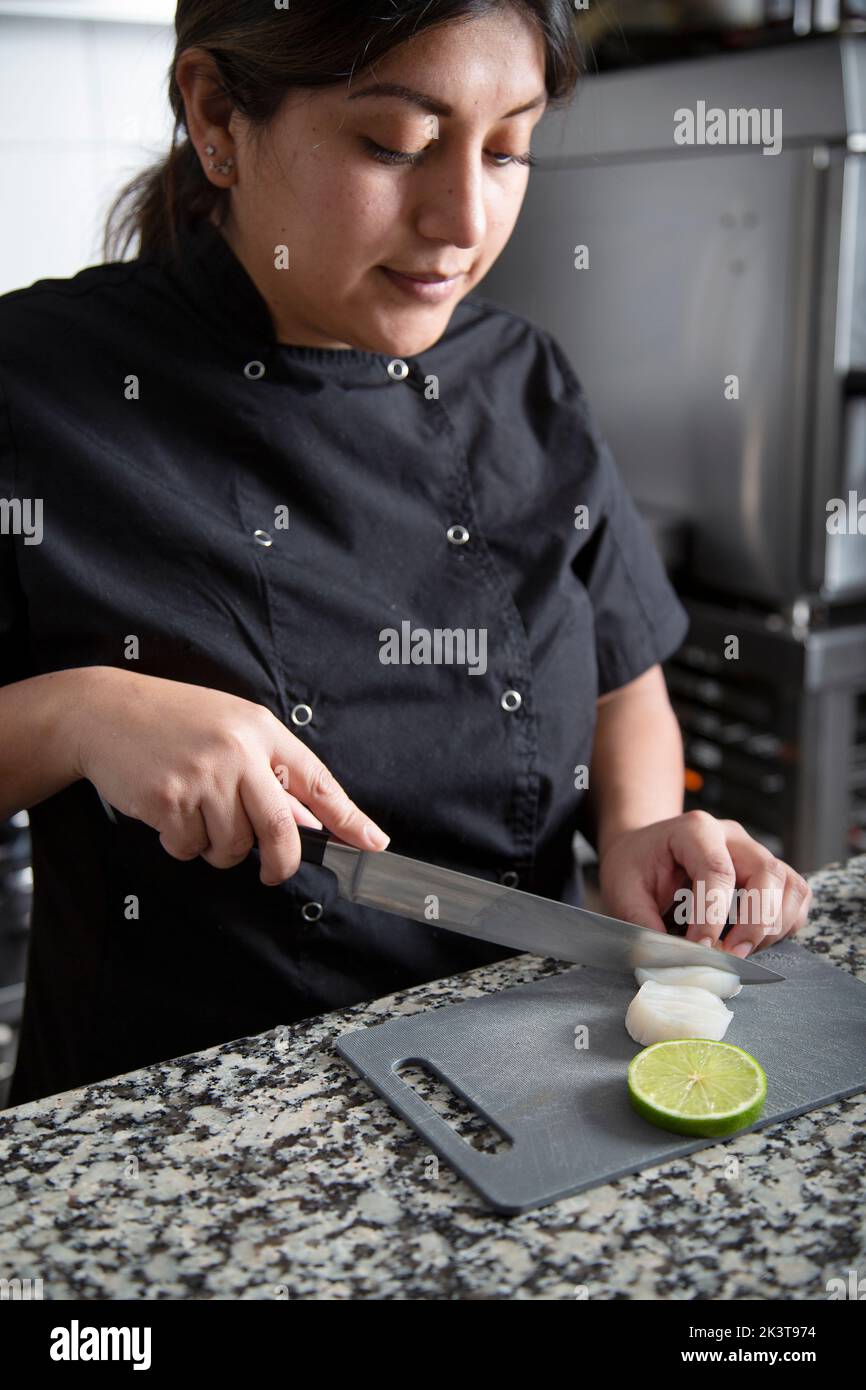 Hispanic female chef cutting white daikon on cutting board with lime ...
