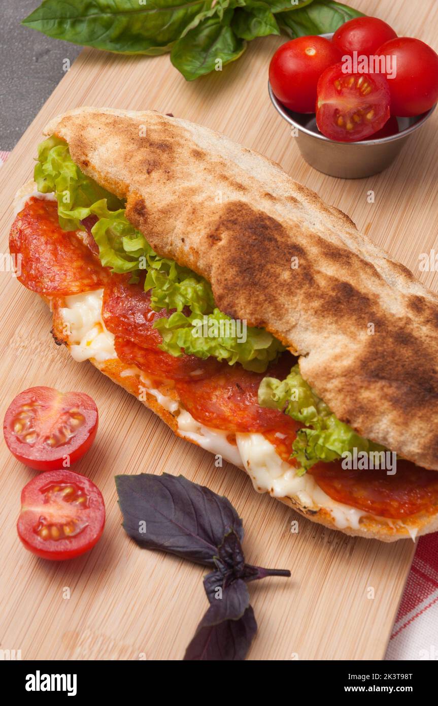 tasty pepperoni panini with cream cheese and salad on a wooden board ...