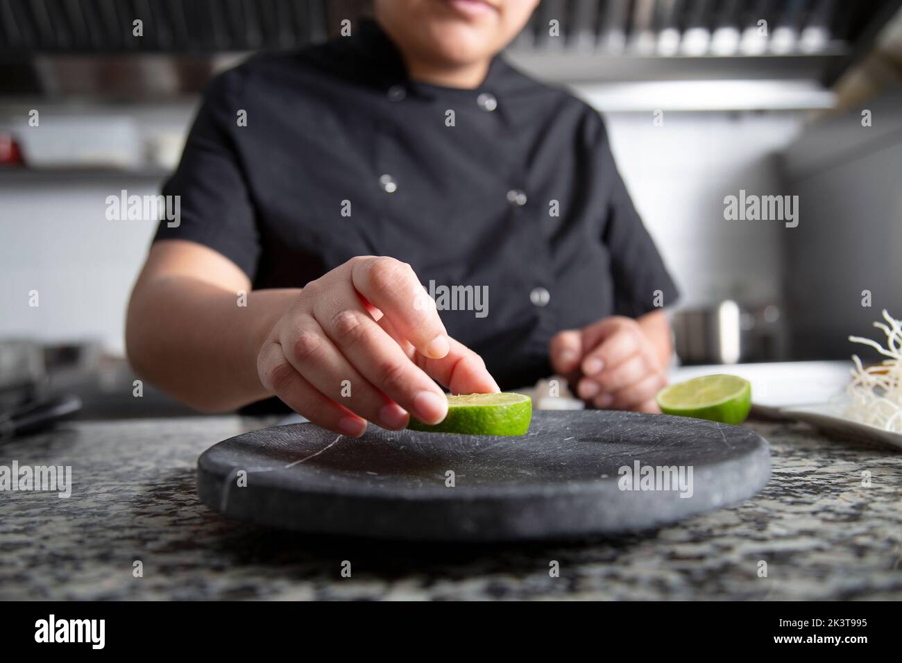 Crop unrecognizable female chef in black uniform putting green lime ...