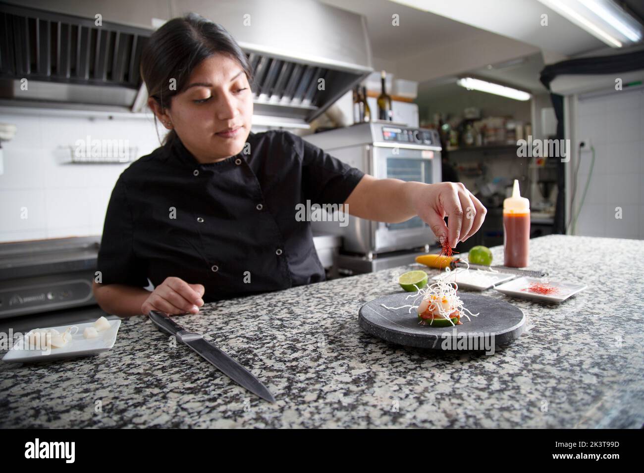 Hispanic female chef putting shredded white daikon on snack with ...