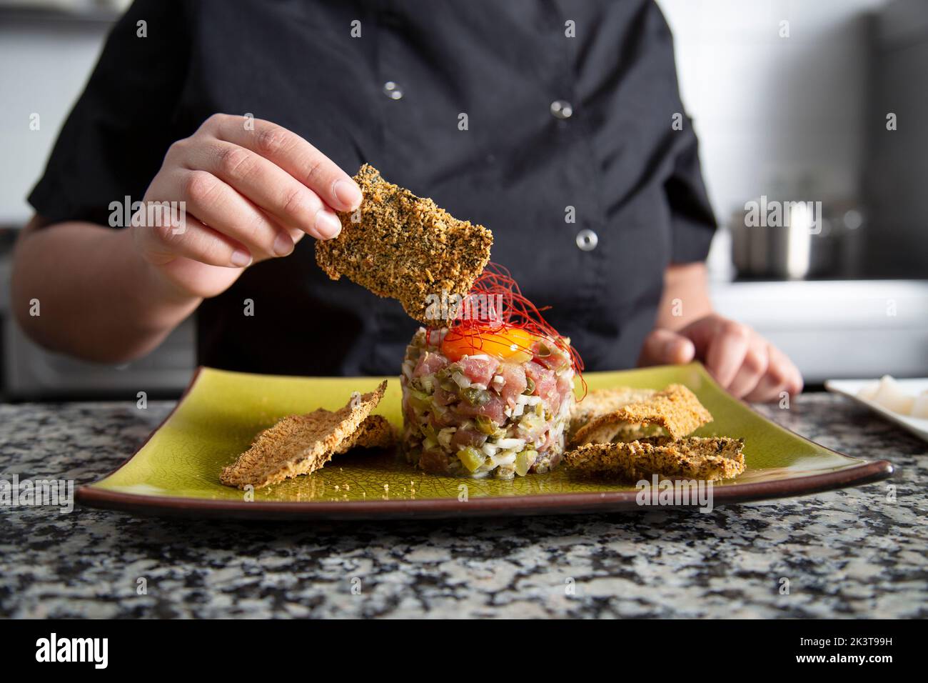 Crop anonymous female chef putting crouton on plate with tuna tartare ...