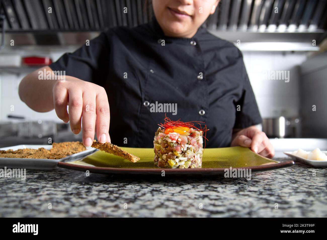 Crop anonymous female chef putting crouton on plate with tuna tartare ...