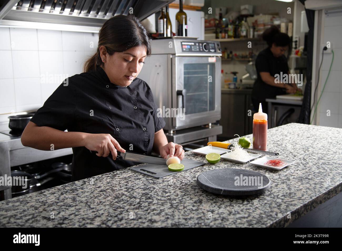 Hispanic female chef cutting white daikon on cutting board with lime ...