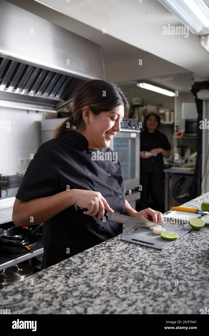 Happy hispanic female chef cutting white daikon on cutting board with ...