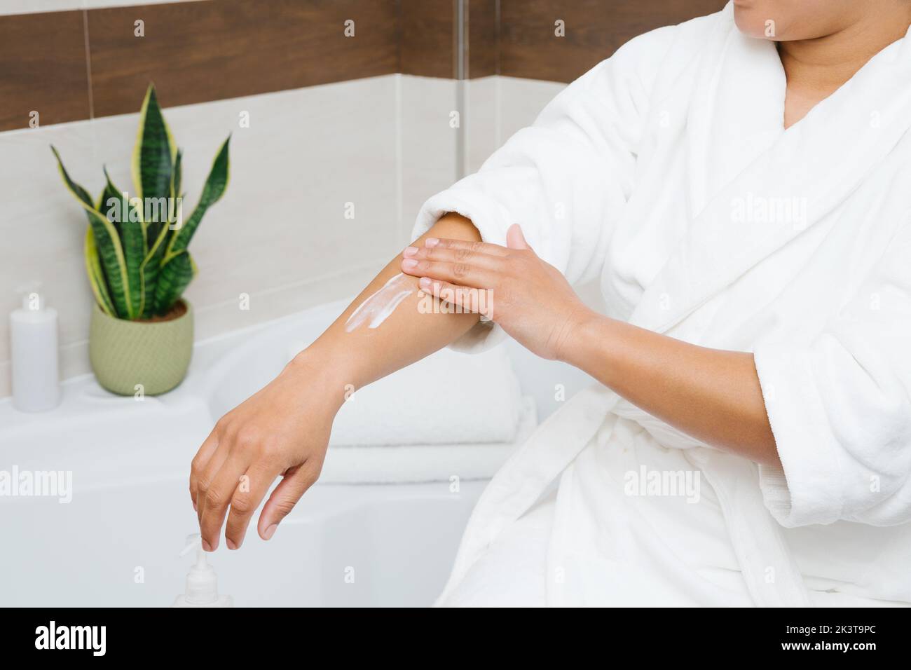 Cropped unrecognizable female applying moisturizing body cream on arms ...