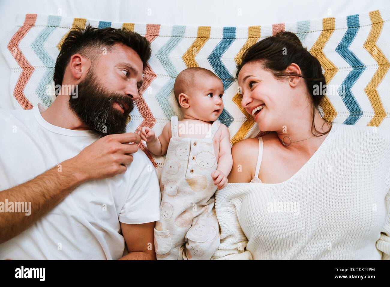 From above serene baby lying on bed among mother and father cuddling ...