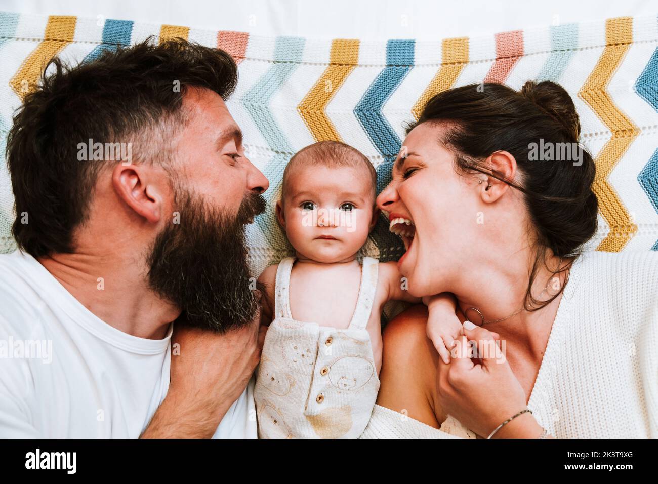 From above serene baby lying on bed among mother and father cuddling ...