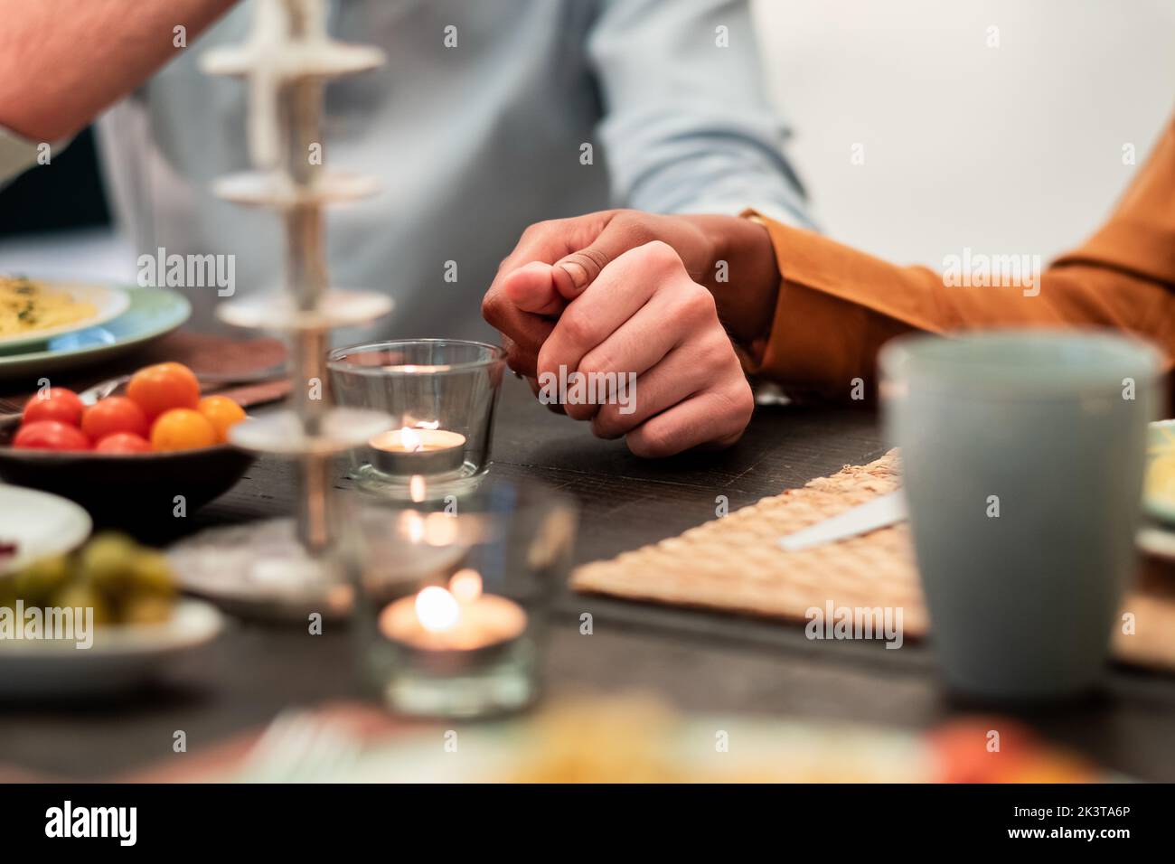 Crop multiracial couple holding hands while sitting together at table ...