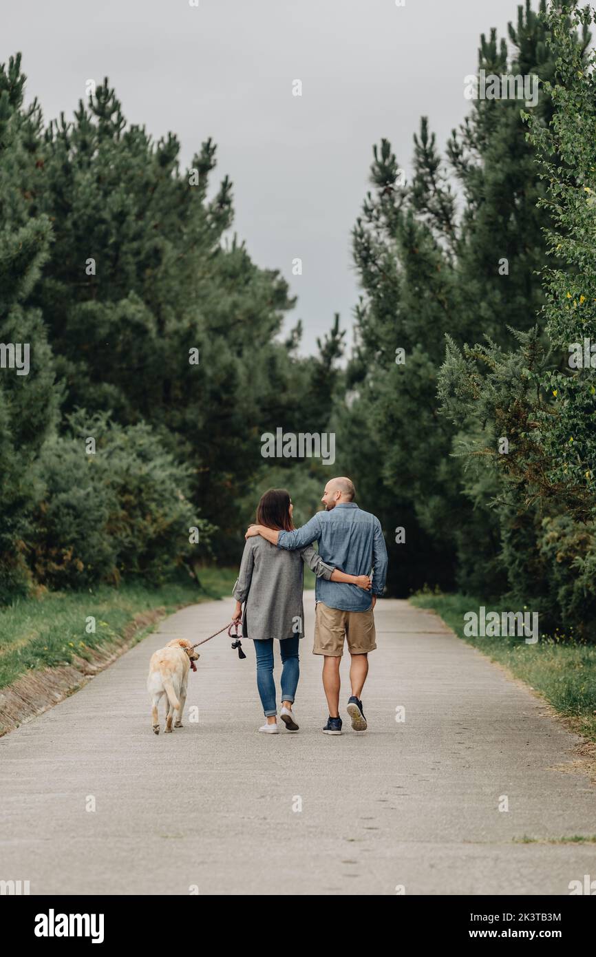 Happy couple in casual wear walking with dog on wood paved road in ...
