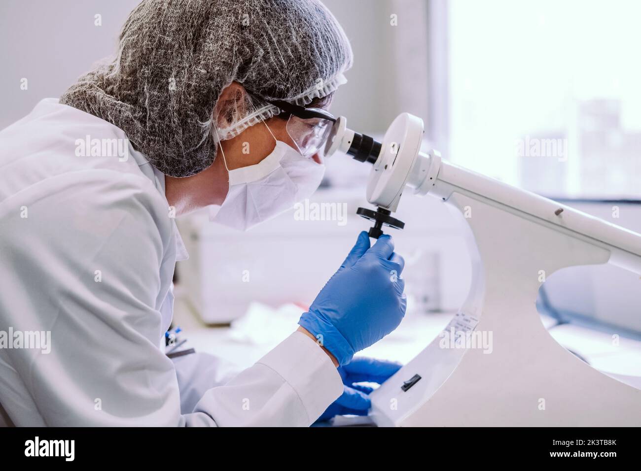 Side view of woman looking in microscope while working in laboratory ...