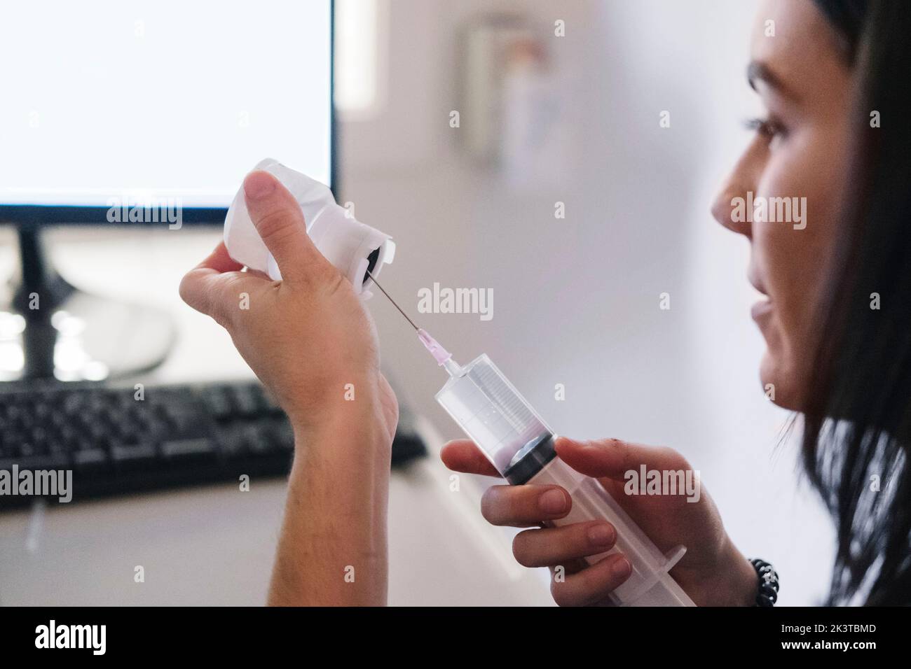 Side view of young female doctor filling in syringe with medicine from ...