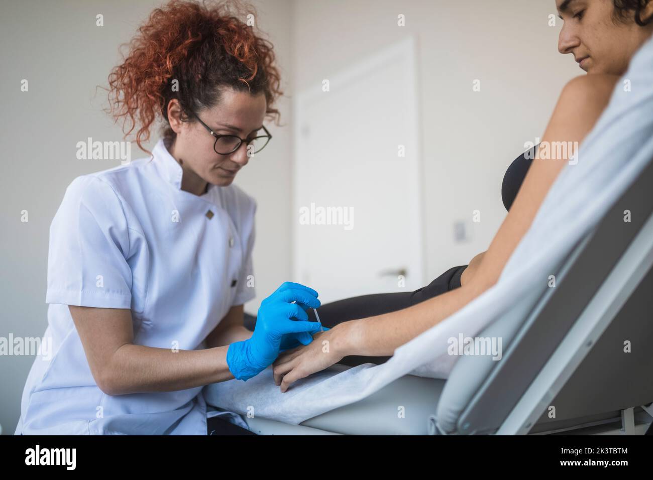 Skilled female physiotherapist in medical uniform and gloves treating ...