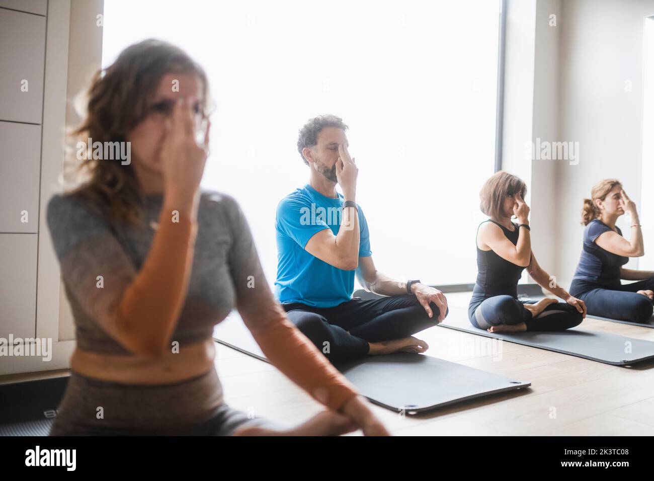 Group of concentrated people in activewear sitting with legs crossed and keeping fingers in ...