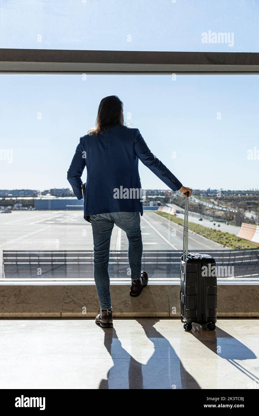 Man in stylish outfit holding laptop and looking away while standing ...