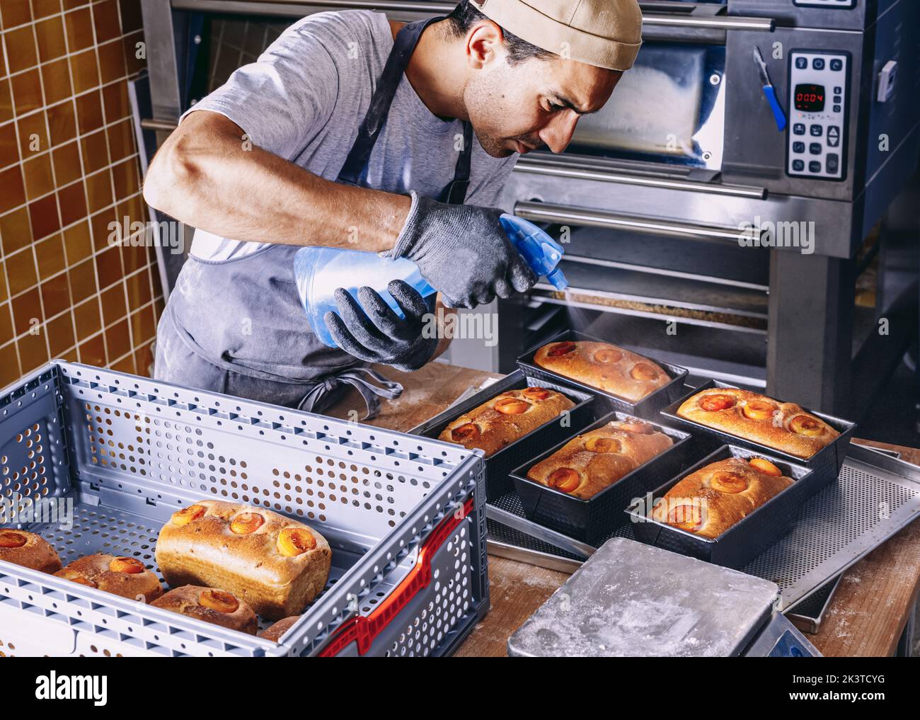 Male baker in apron standing in bakery kitchen and preparing raw bread ...