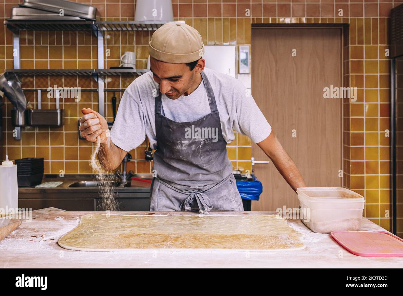 Focused ethnic male baker in dirty apron standing at table in bakehouse ...