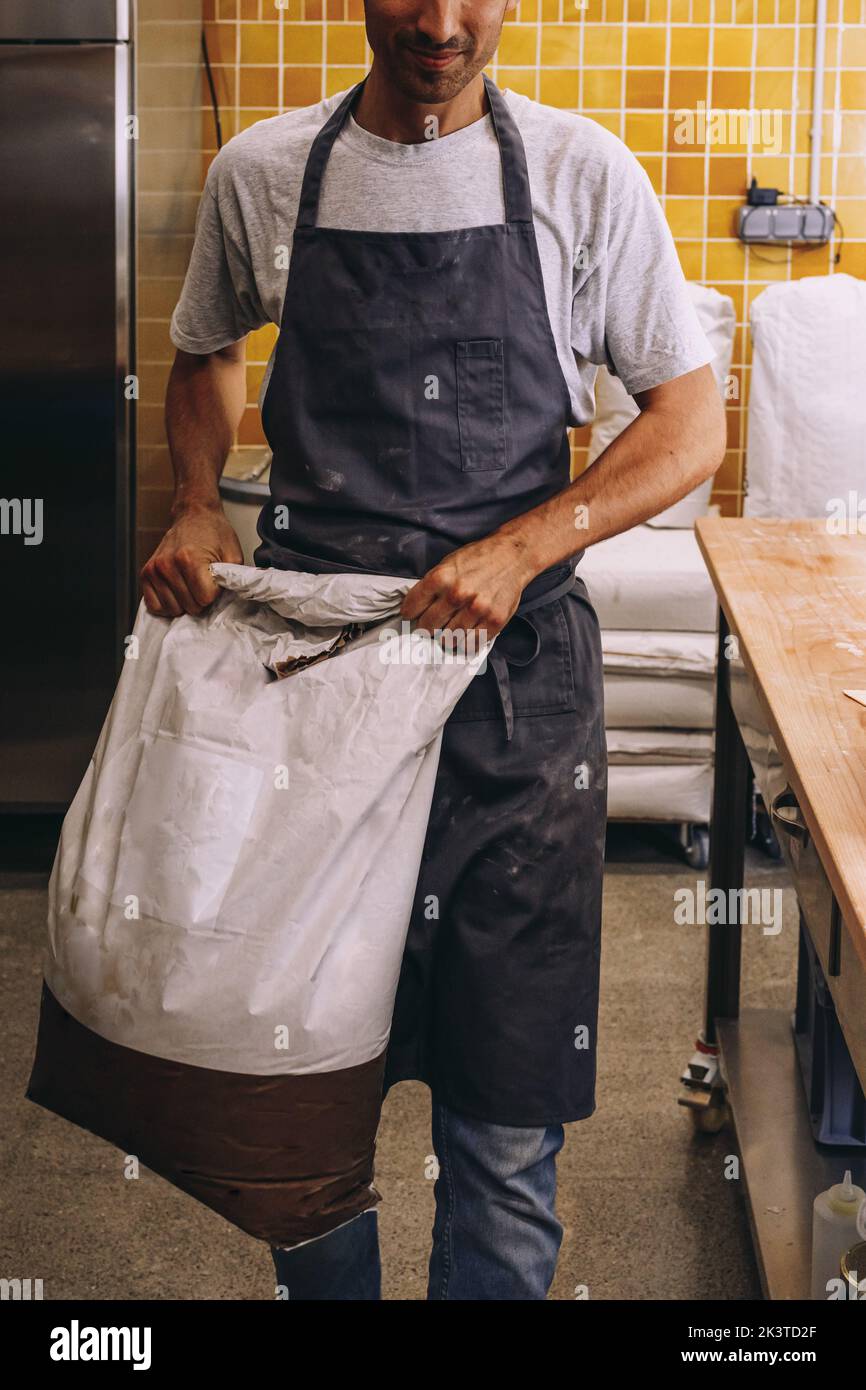 Crop unrecognizable male worker in apron carrying big sack with ...