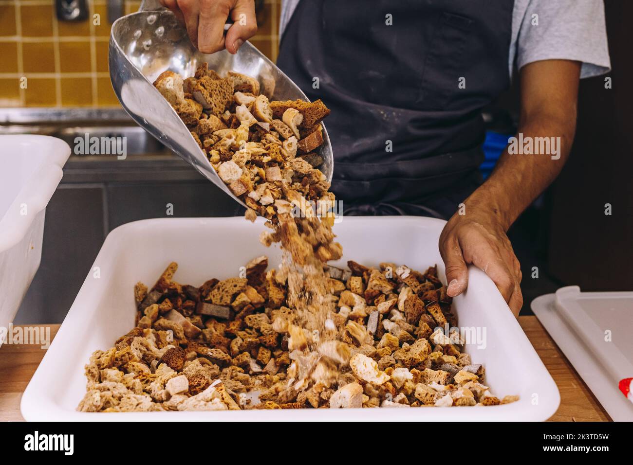 Crop anonymous male baker in apron spilling dried bread crumbs into ...