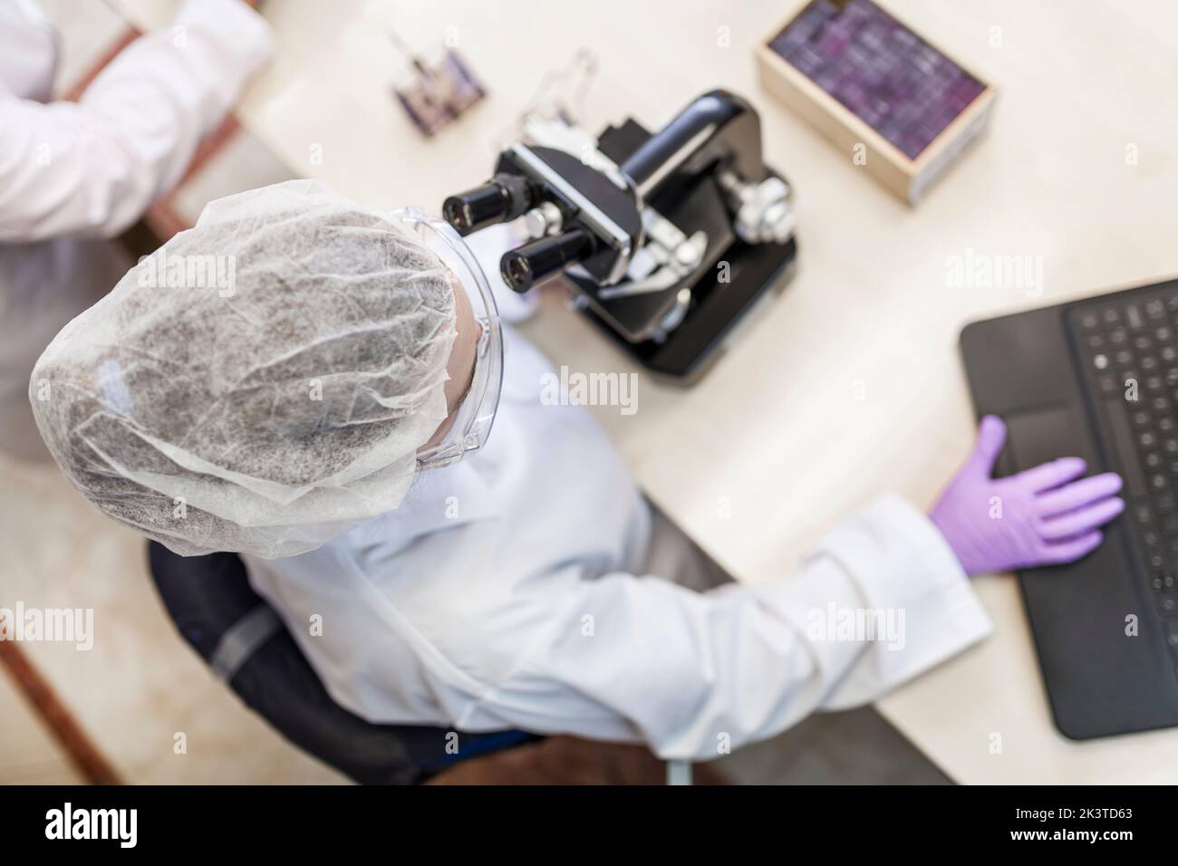 From above woman scientist looking through microscope at laboratory ...