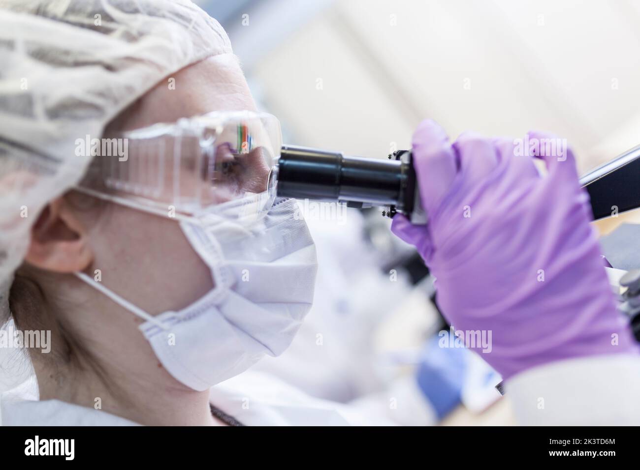 close-up side view of woman scientist looking through microscope at ...
