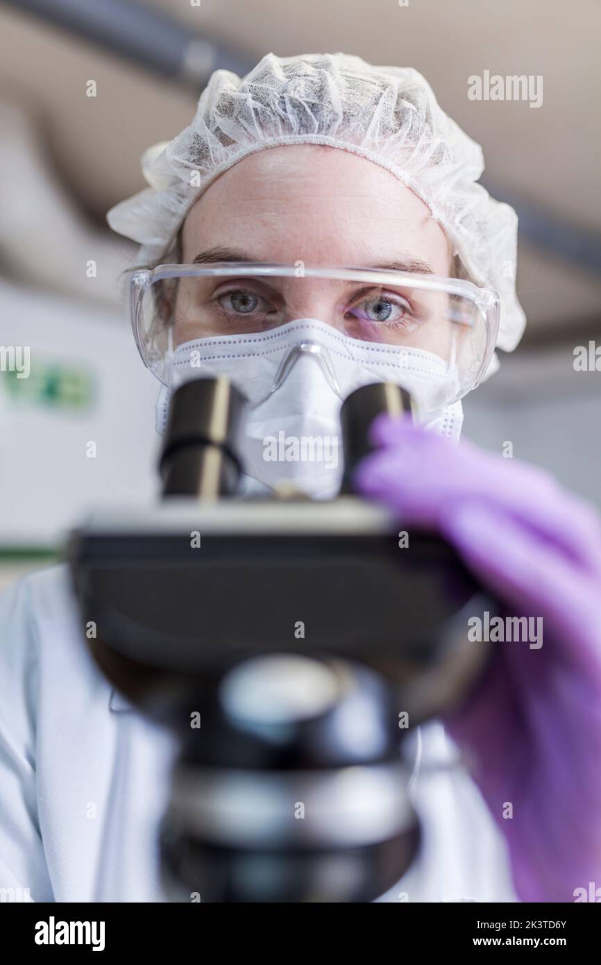 close-up front view of woman scientist looking through microscope at ...