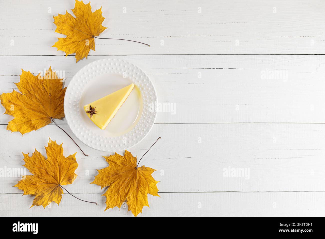 Pumpkin pie piece on white plate with fall yellow maple leaves on white ...