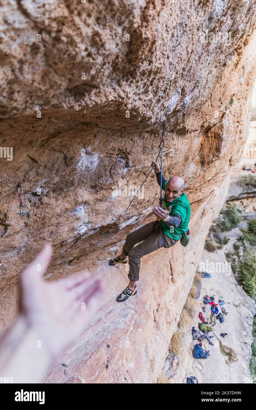 climber offering his hand to another colleague while hanging on a rope ...