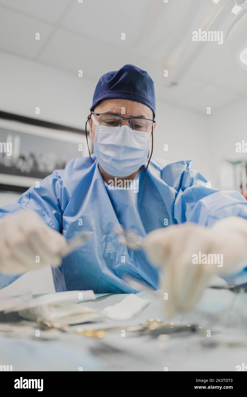 Adult male doctor in uniform and mask choosing instruments in surgery ...