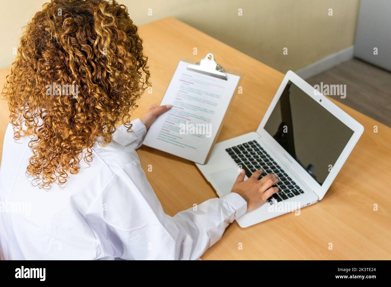 From above back view of anonymous female medic with document typing on ...
