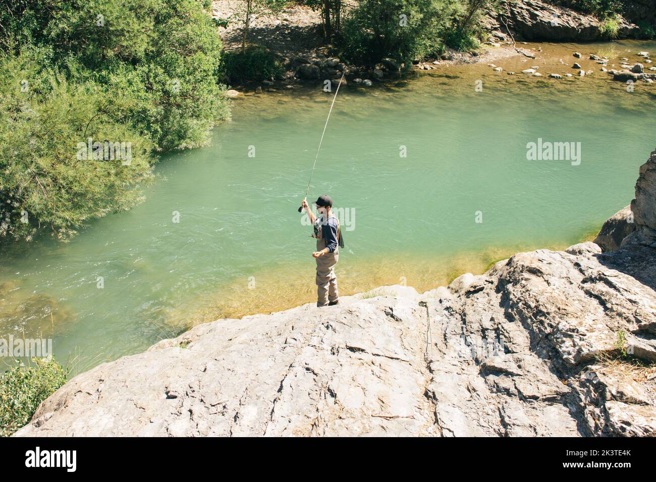 From above male fisherman throwing fishing rod into a mountain river ...