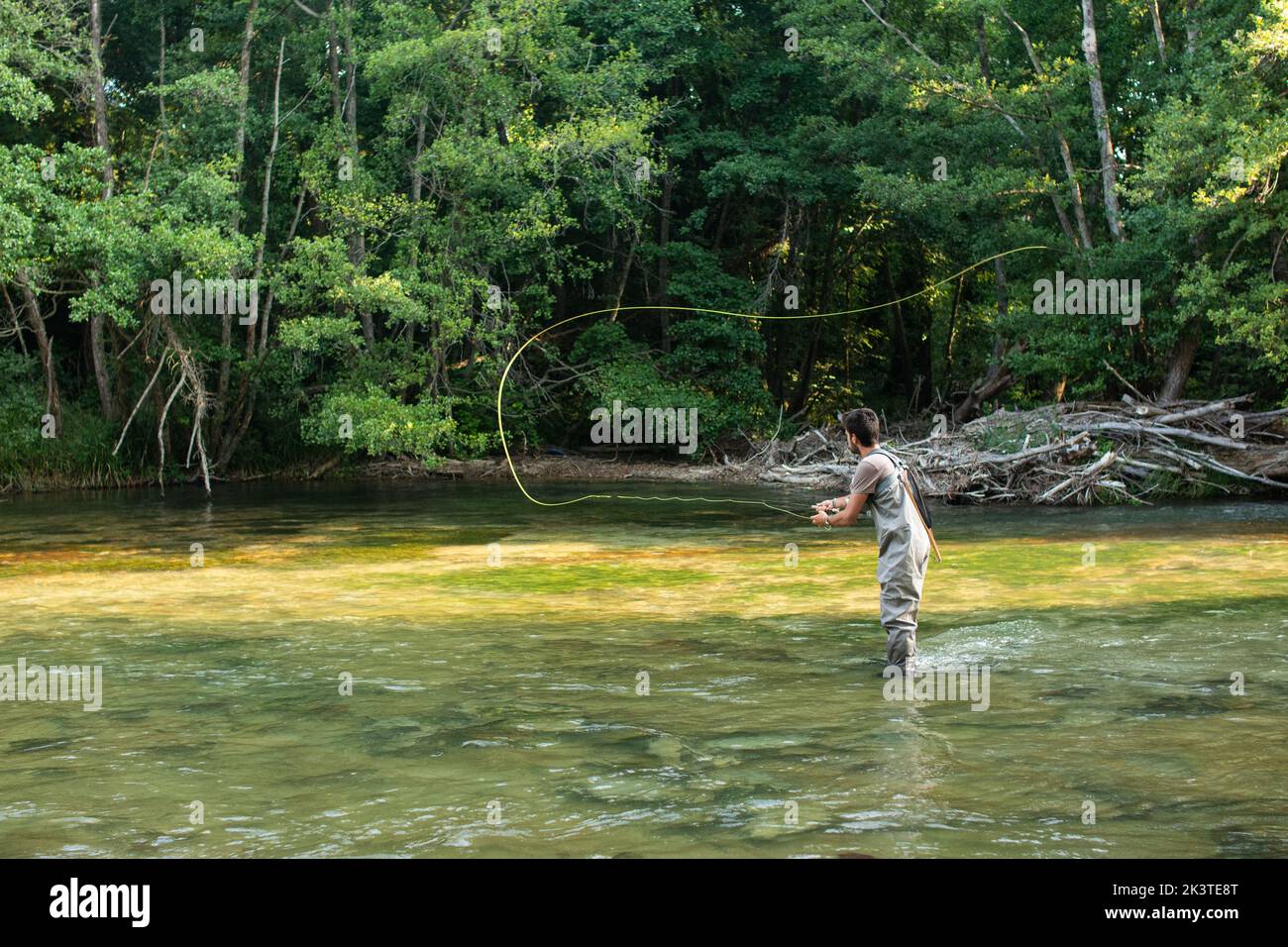 Side view of male fisherman throwing fishing rod into a mountain river ...