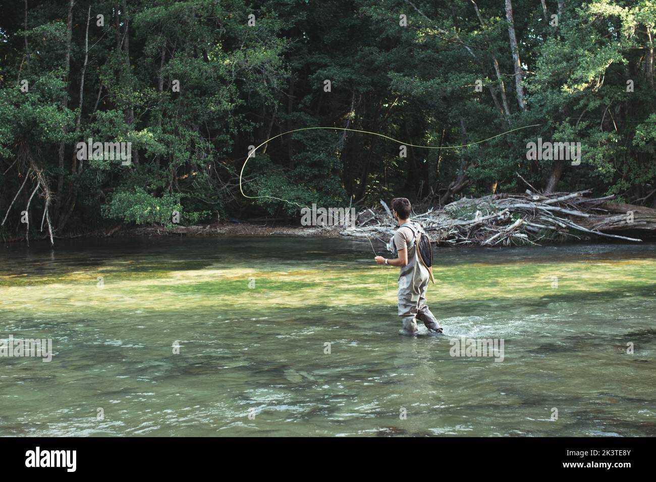 Side view of male fisherman throwing fishing rod into a mountain river ...