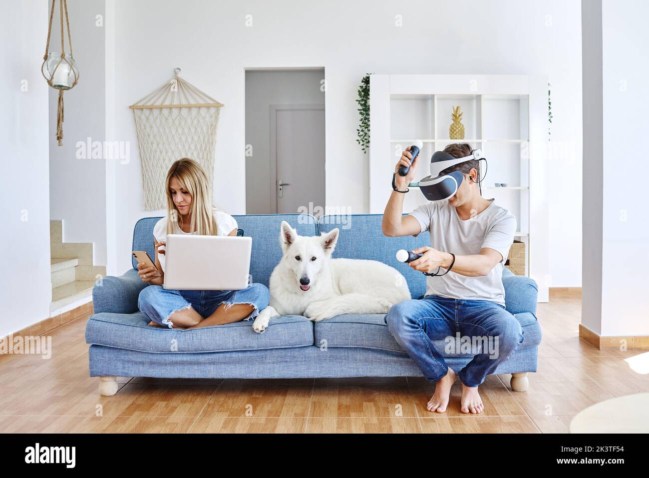 Woman using laptop and smartphone and boyfriend in VR goggles and with ...