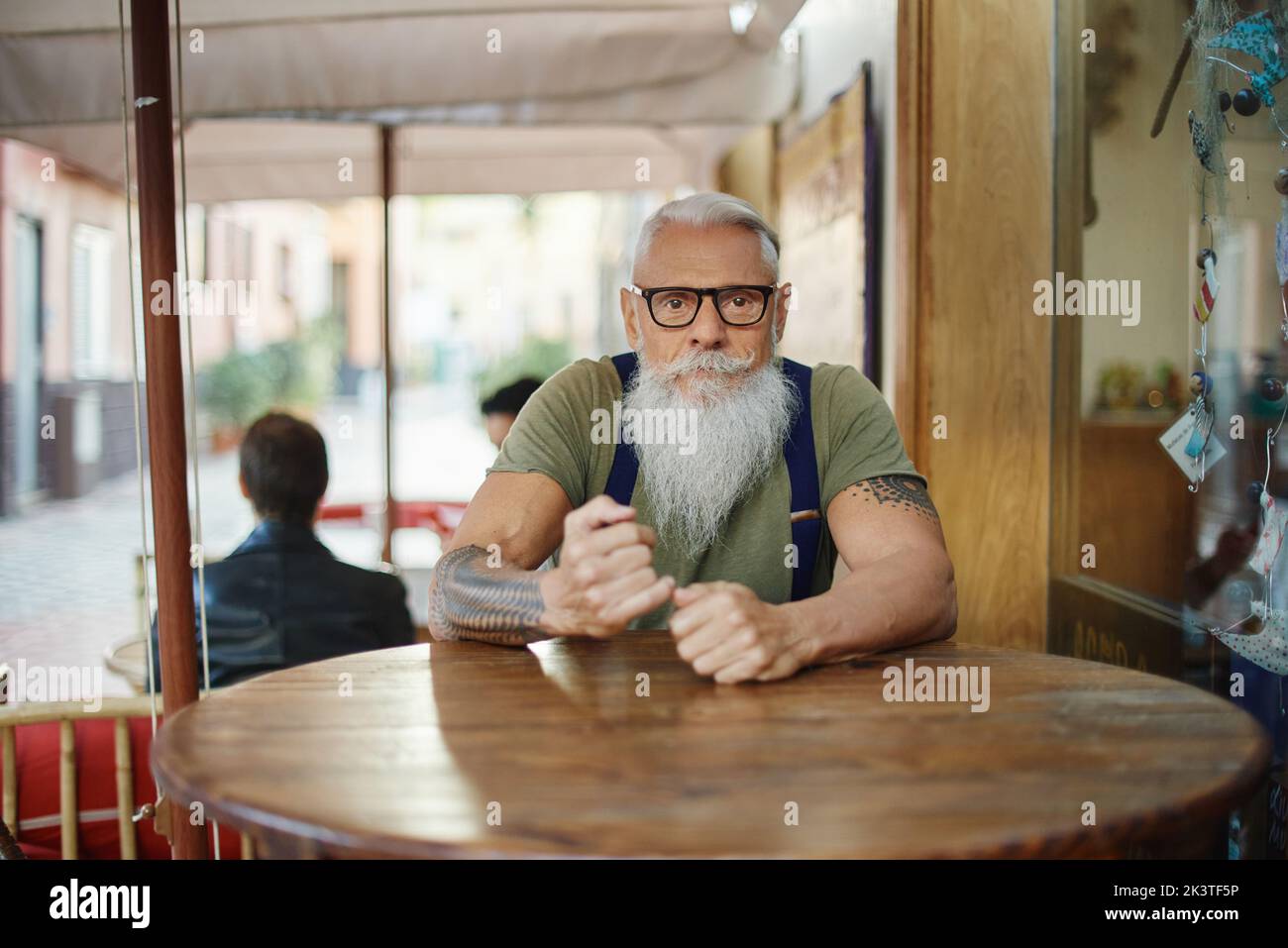 Elderly stylish bearded dandy male with tattoo and glasses looking at ...