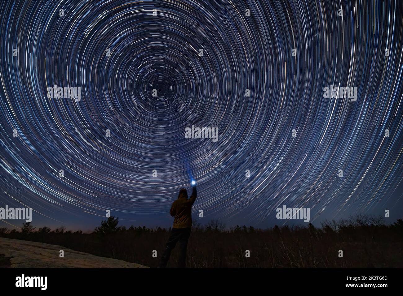 A hooded person shining a light at the sky and making the stars rapidly ...