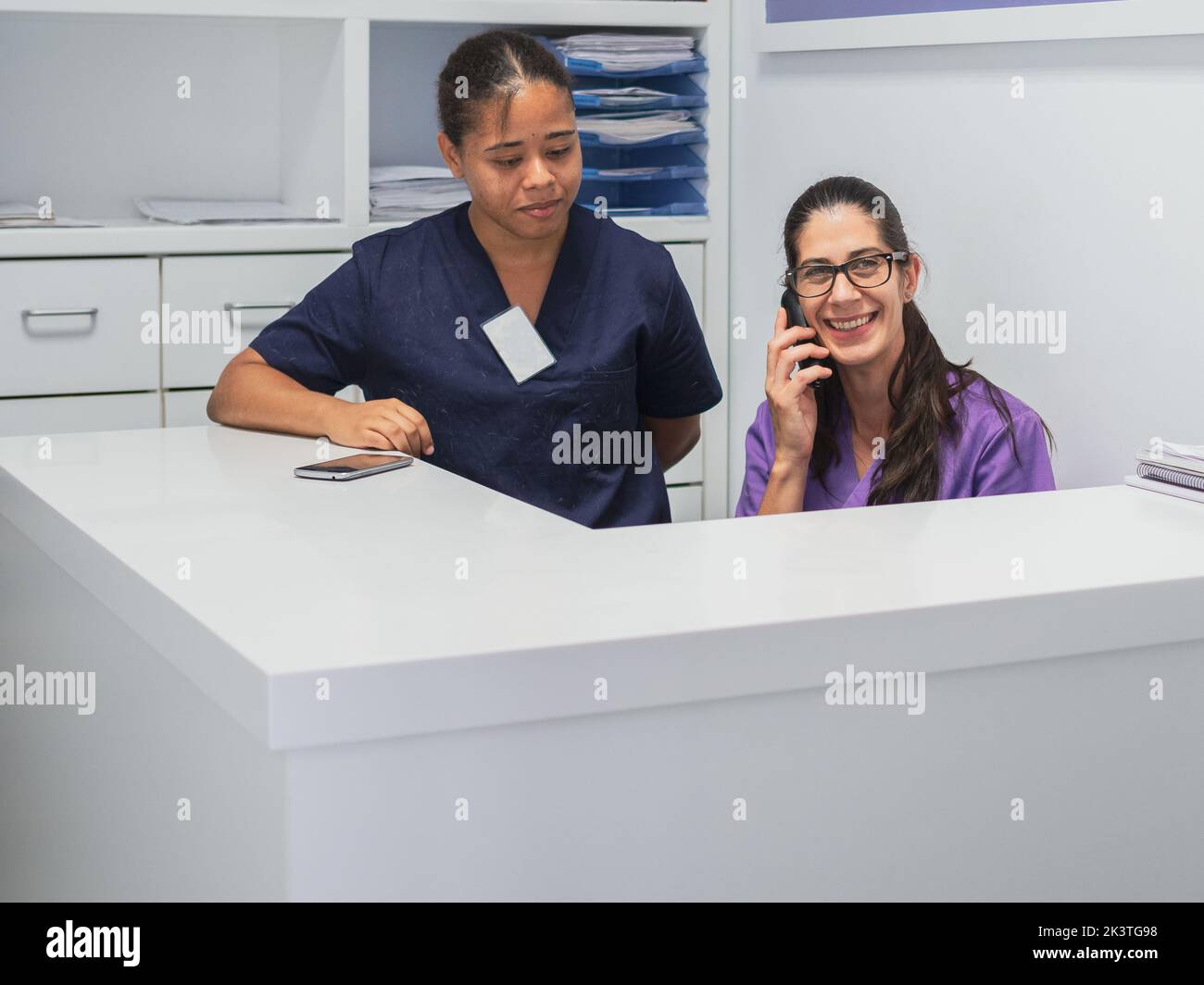 Female nurses in scrubs smiling while working behind counter on ...