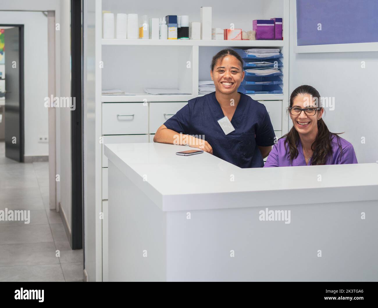 Female nurses in scrubs smiling while working behind counter on ...