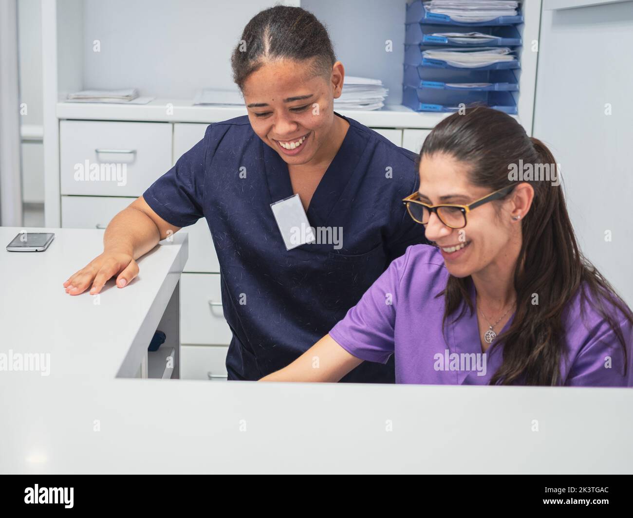 Female nurses in scrubs smiling while working behind counter on ...