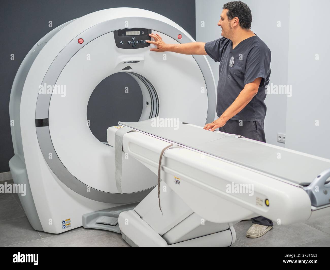Side view of adult man in scrubs pushing buttons on modern MRI scanner ...