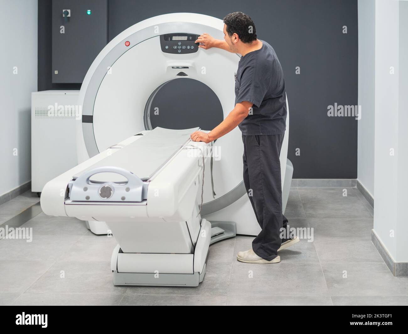 Side view of adult man in scrubs pushing buttons on modern MRI scanner ...
