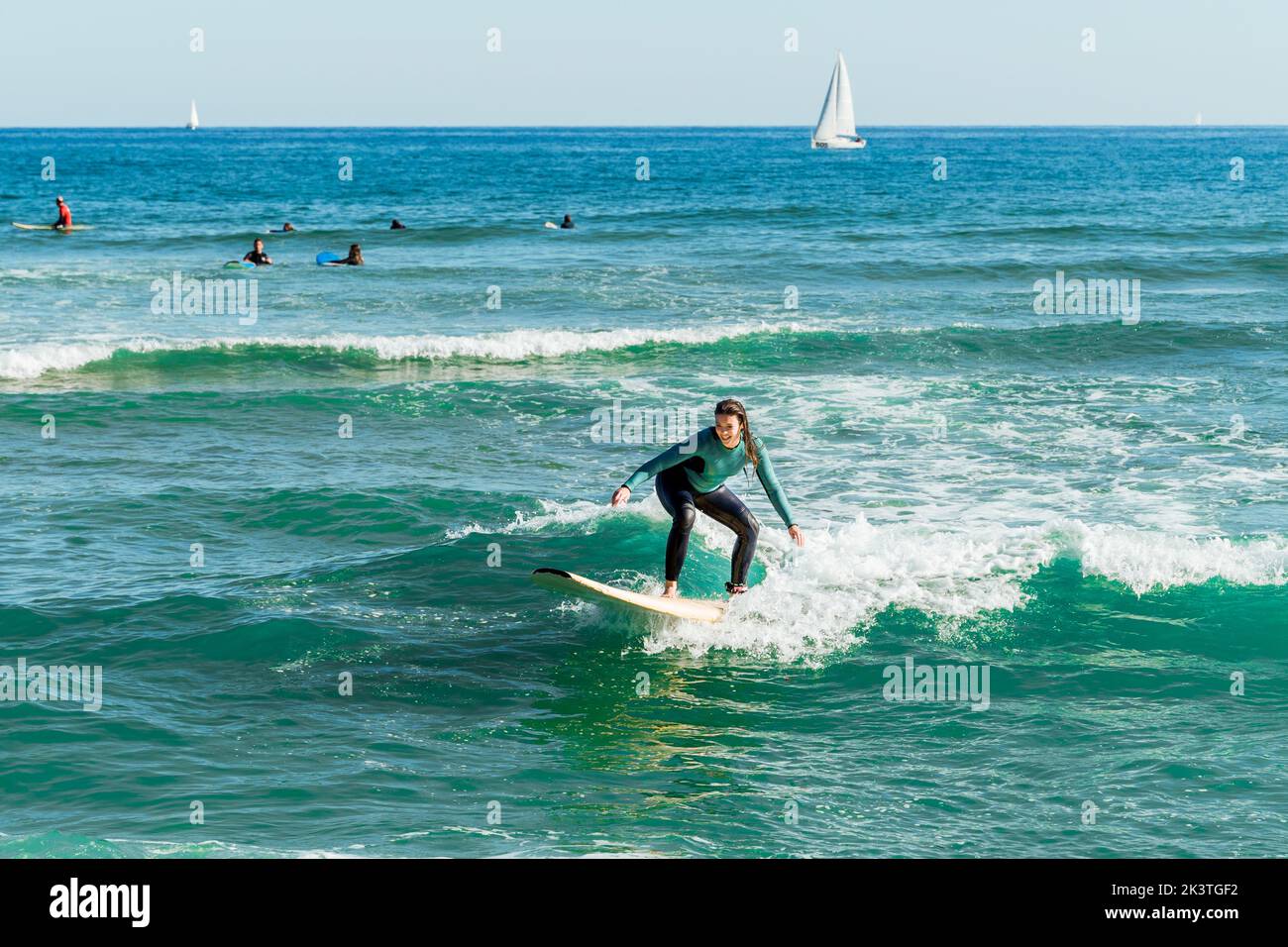Full length of young female surfer in wetsuit riding surfboard on wavy ...