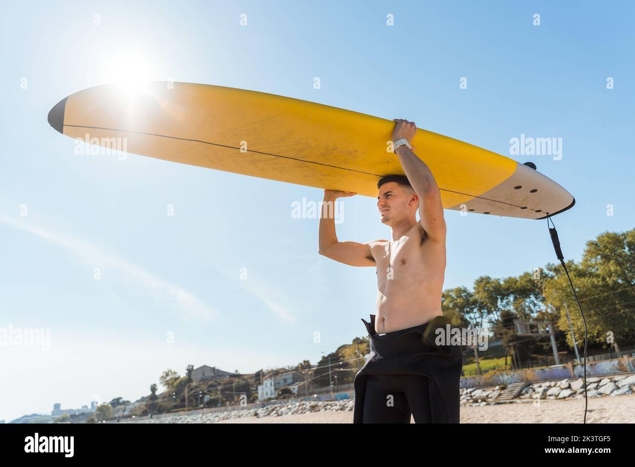 From below young surfer man dressed in wetsuit standing looking away on ...