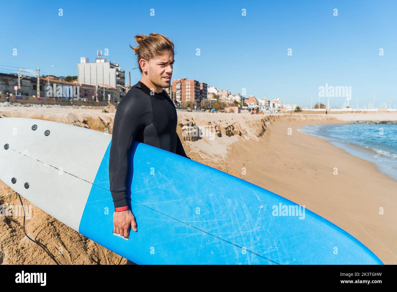 Side view of young thoughtful male with surfboard in hands standing on ...