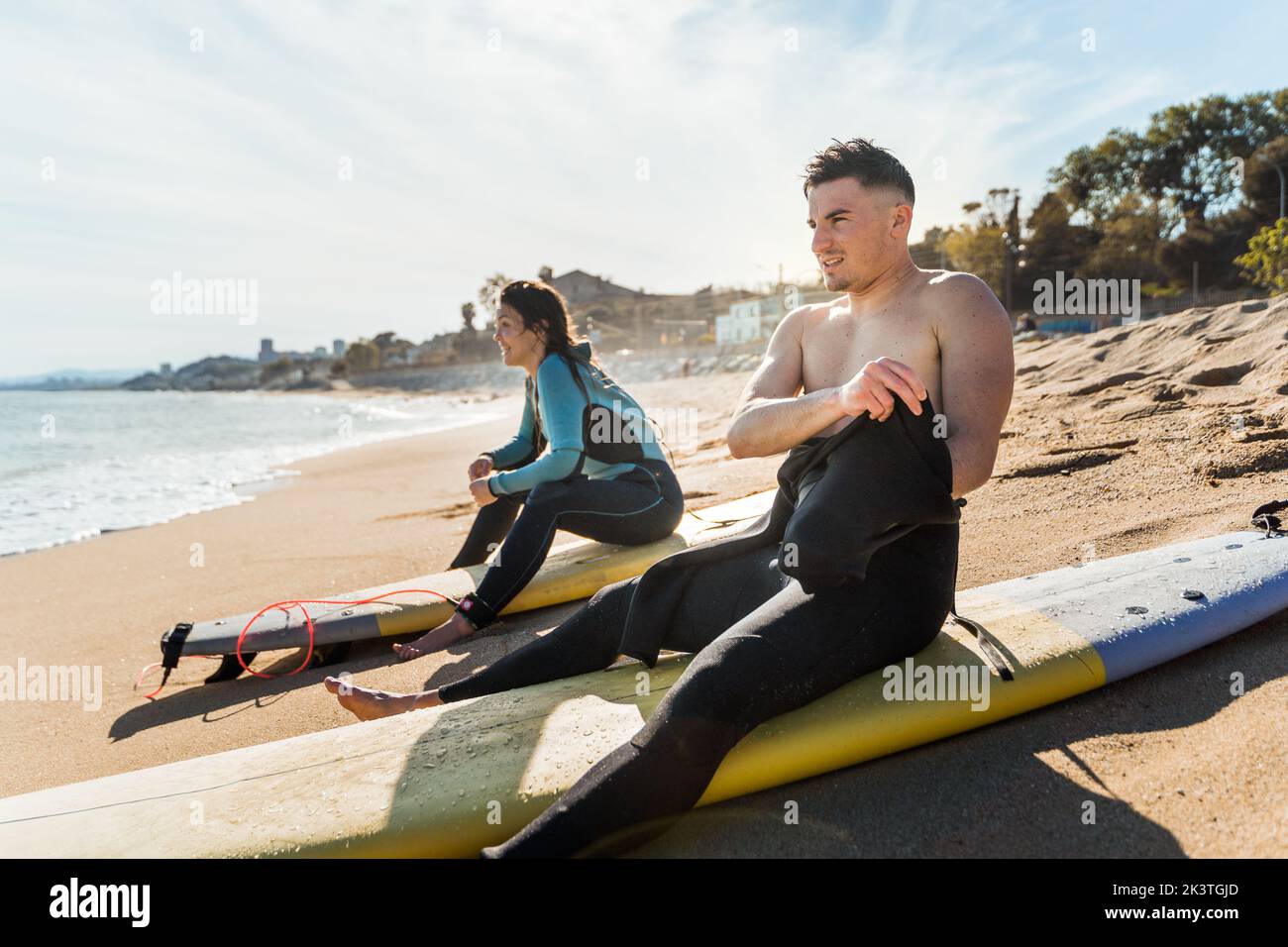 Side view of young sporty man and woman in wetsuits sitting on ...