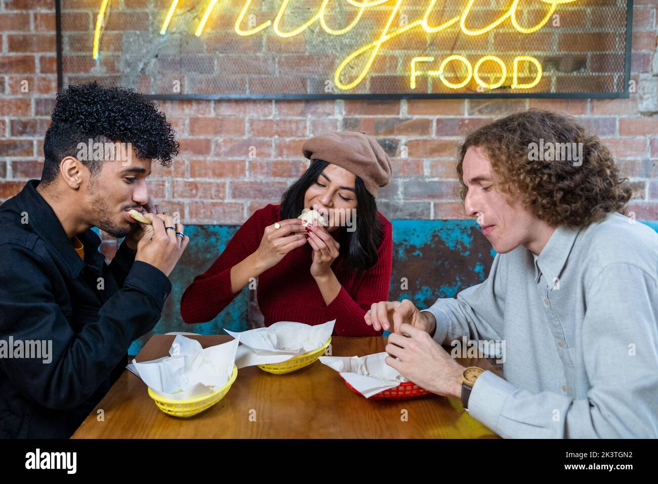 Young multiracial partners eating tasty tacos at wooden table in ...