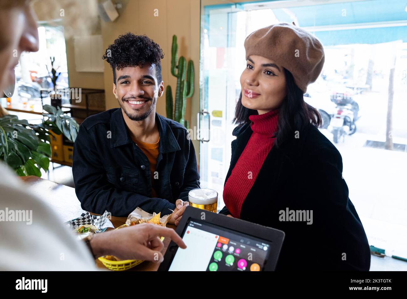 Young ethnic couple ordering food and talking to male server standing ...