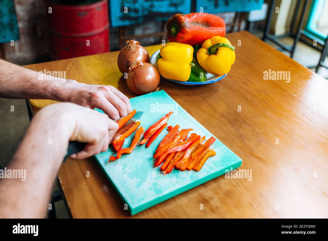 Crop anonymous chef cutting ripe sweet pepper on chopping board while ...