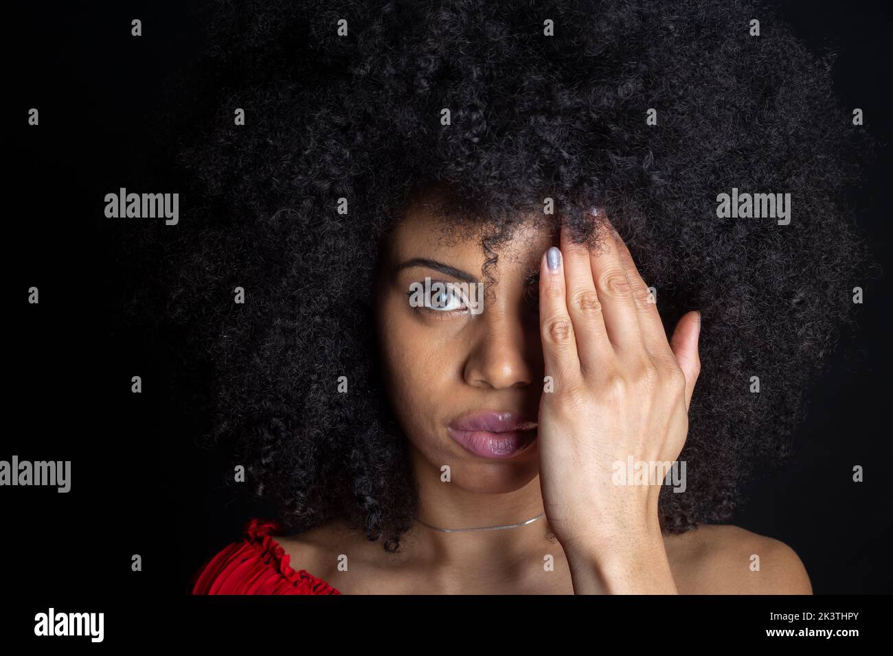 Young unemotional Cuban female with Afro hairstyle covering eye while ...