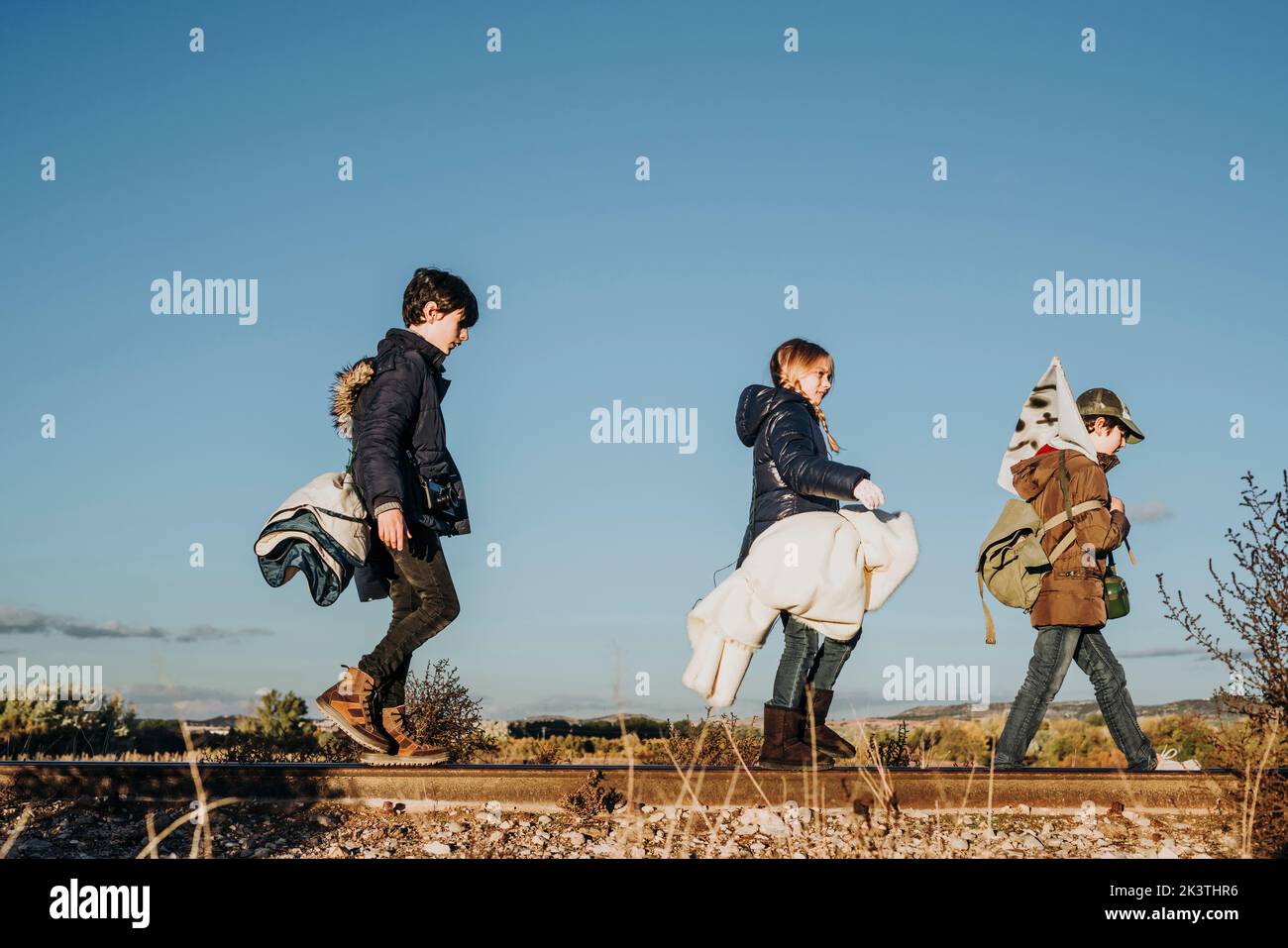 Group of three children hiking in the woods walking in a train track ...
