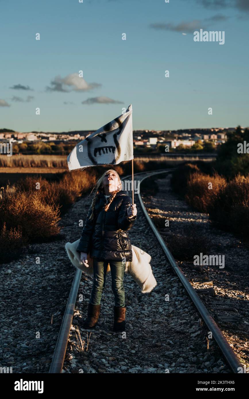 Little girl hiking in the woods caring a sleeping bag and a flag while ...